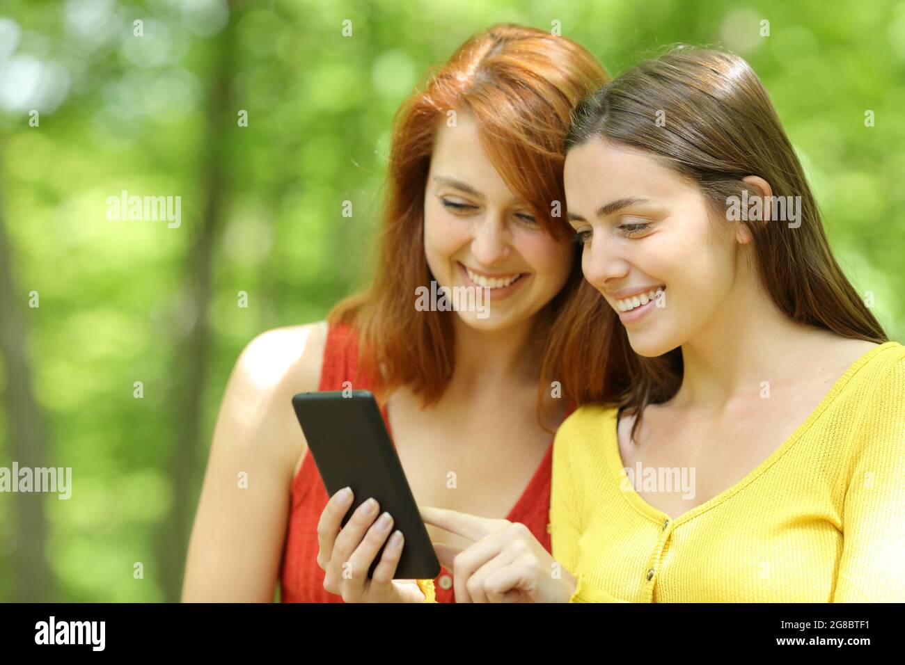 Two happy friends checking smart phone standing in a green park Stock ...