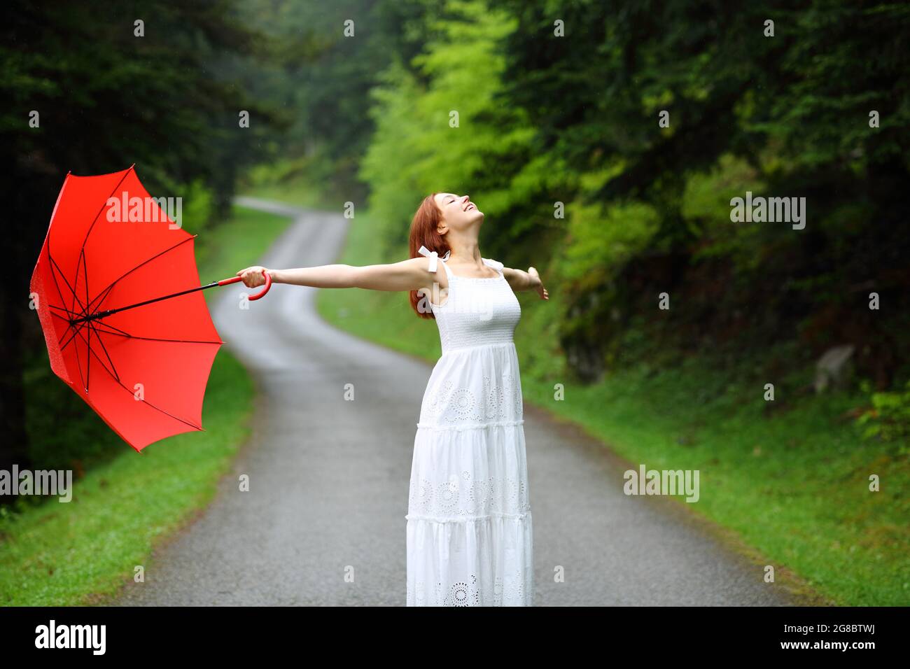 Happy Woman In White Dress Holding Red Umbrella Enjoying Under Rain In