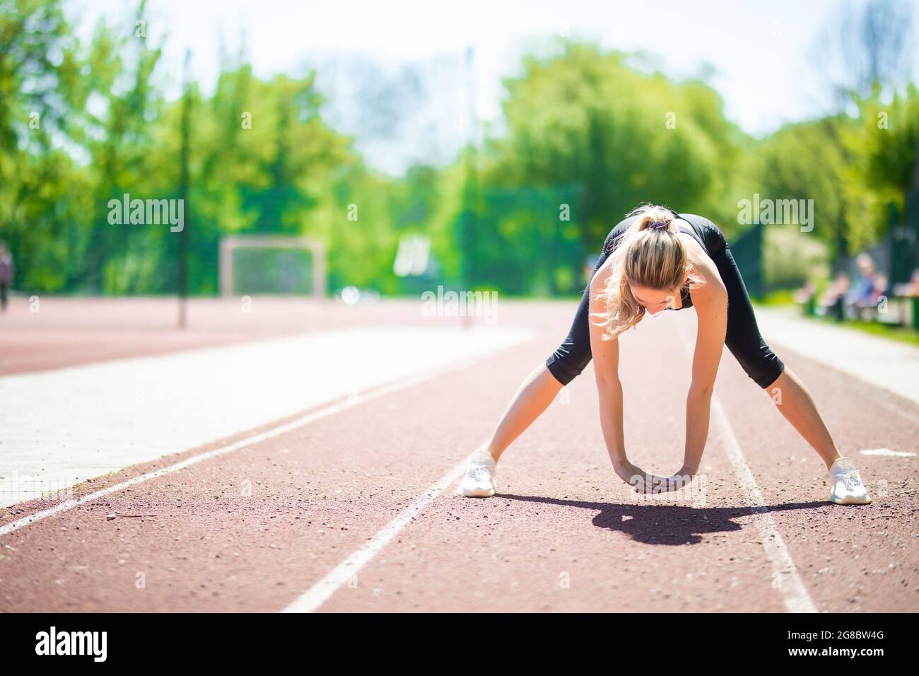 Sprinter woman in sportswear doing warm-up exercises before run on ...