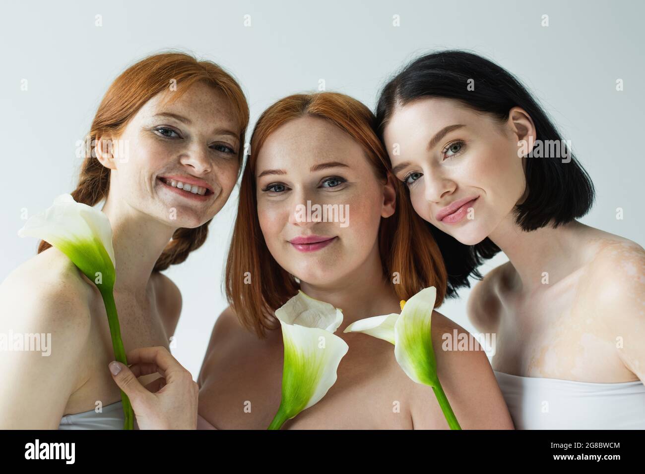Smiling body positive women holding calla lilies isolated on grey Stock ...