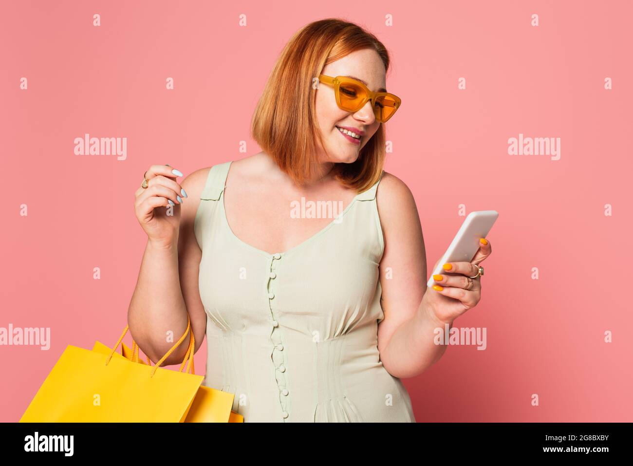 Smiling plus size woman in sunglasses using smartphone and holding ...