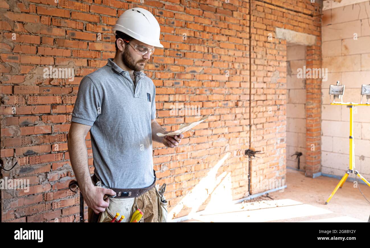 A builder in work clothes examines a construction drawing at a ...
