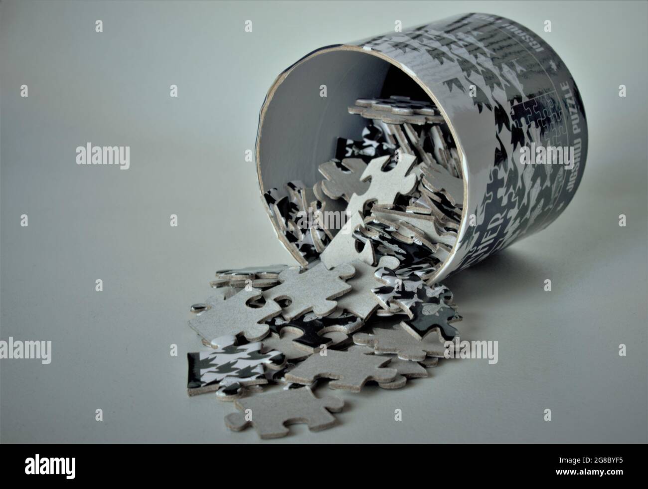 Black and white puzzle pieces fall out of their round box and are ...