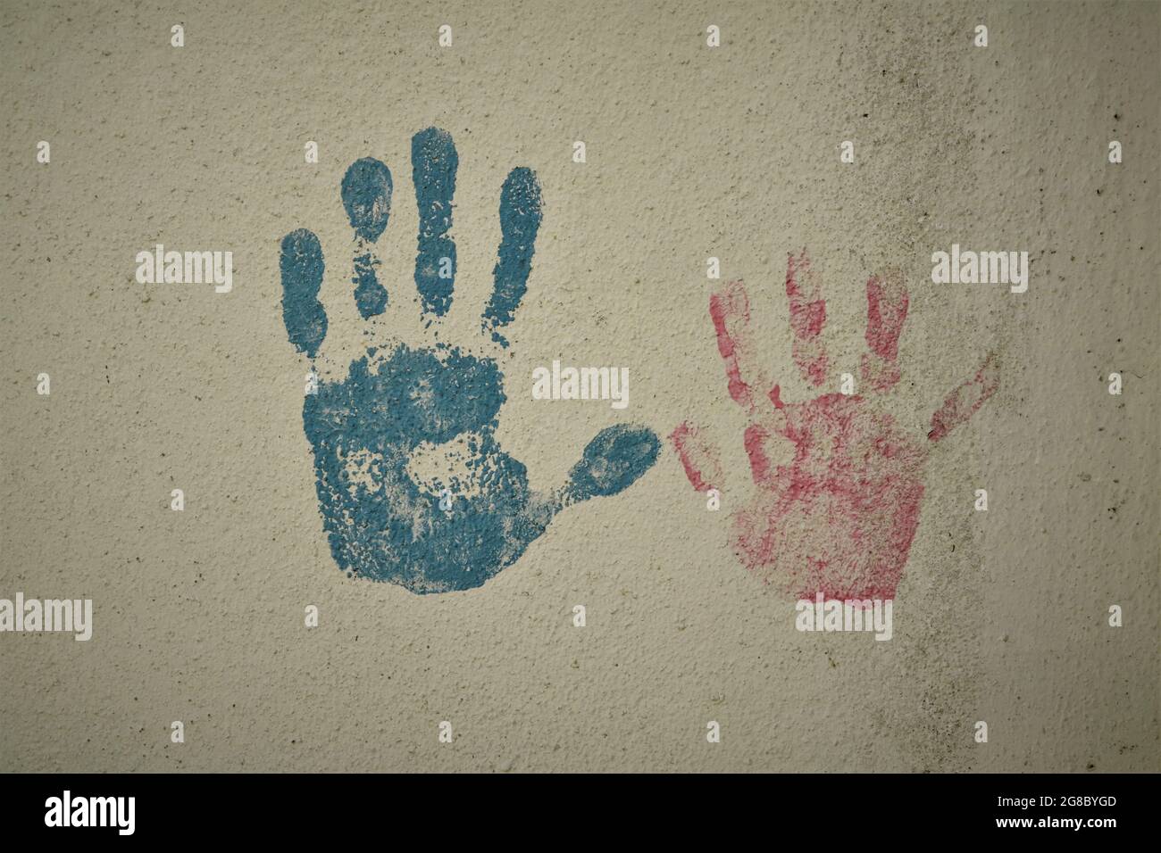 Two hand prints in paint, one big and one small, on a dirty white wall ...