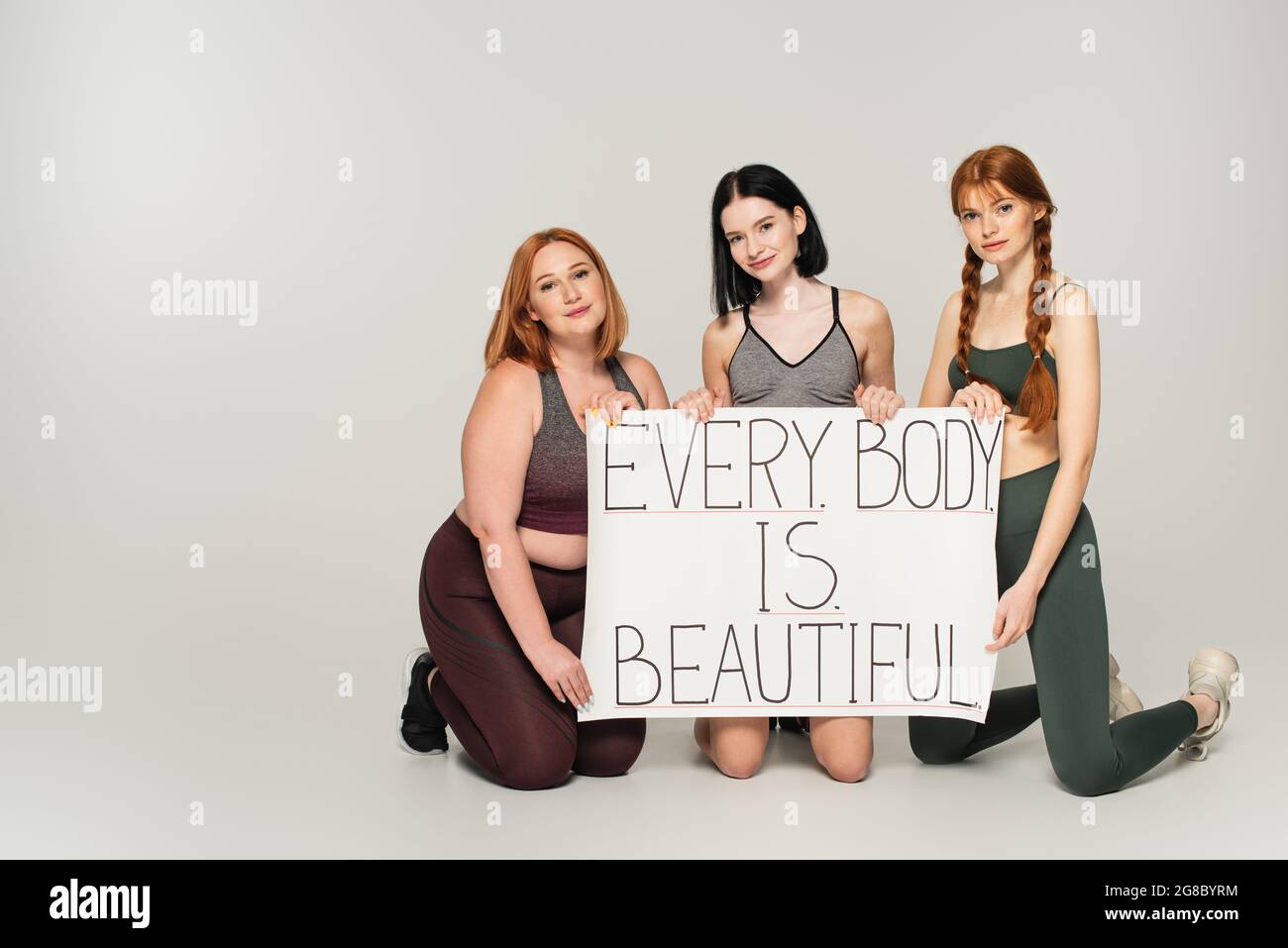 Body positive women in sportswear holding placard with every body is ...