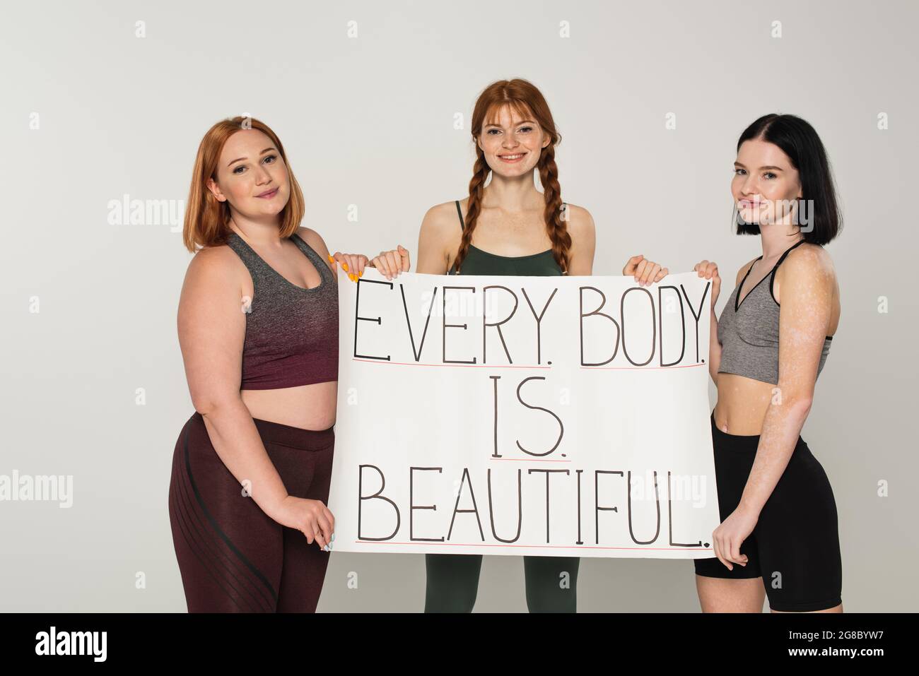 Smiling body positive sportswomen holding placard with every body in ...