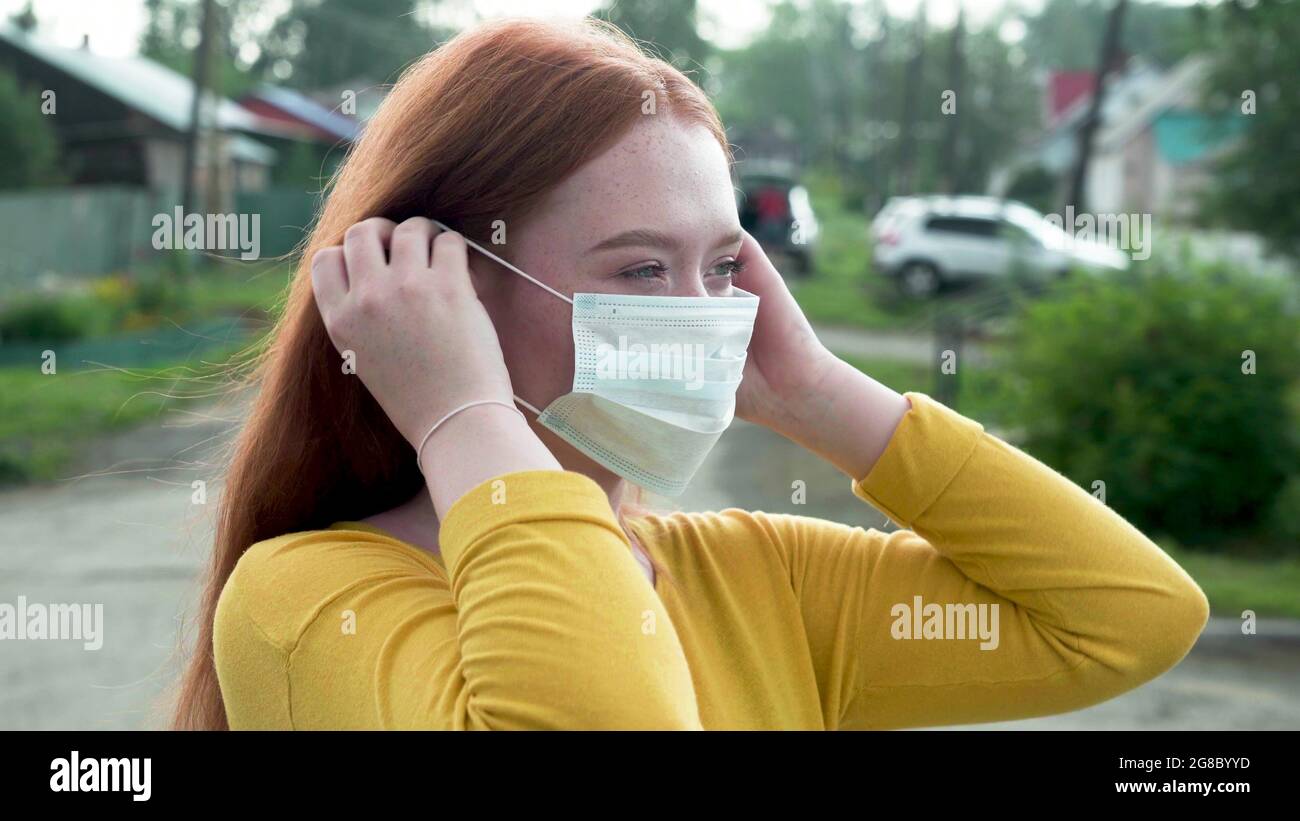 Redhead girl with freckles puts on a medical mask while standing on the ...