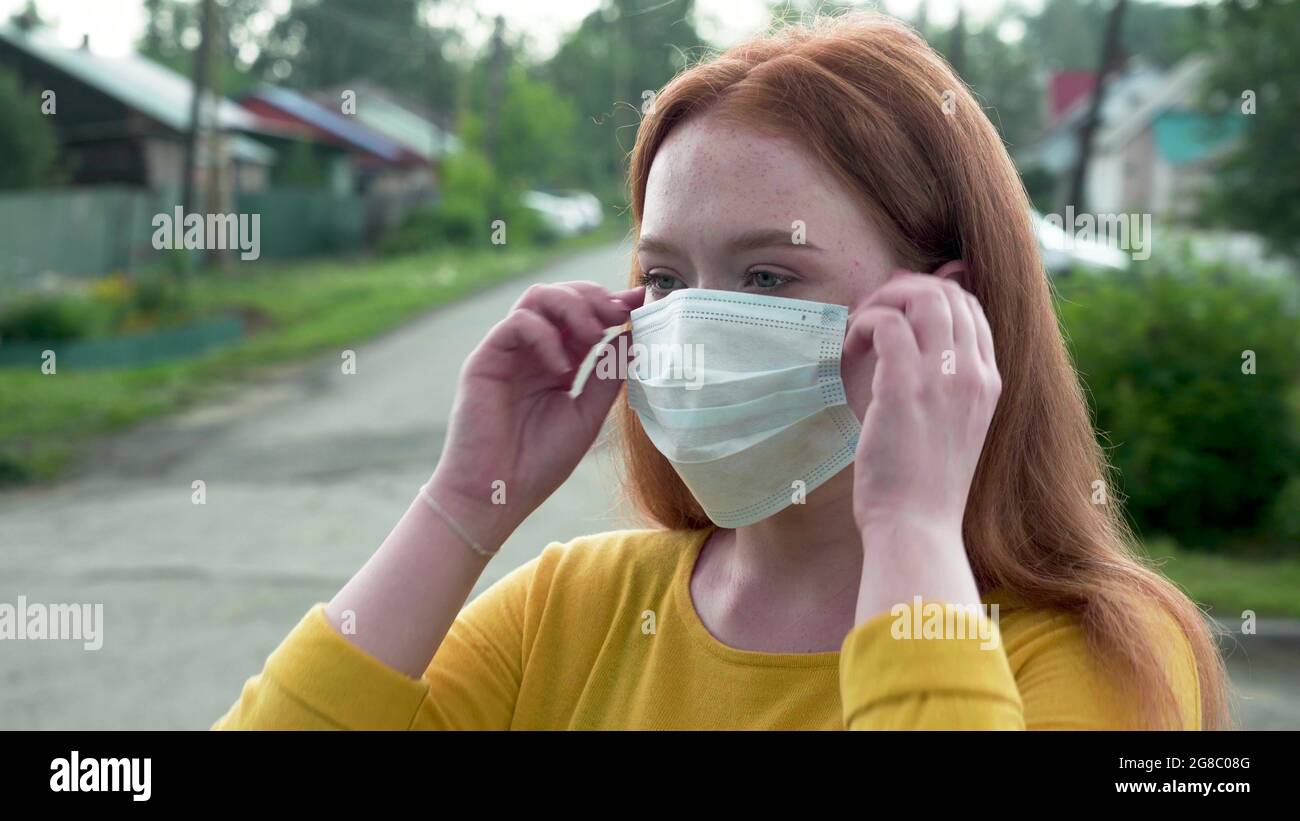 A red-haired girl with freckles takes off a medical mask from her face ...