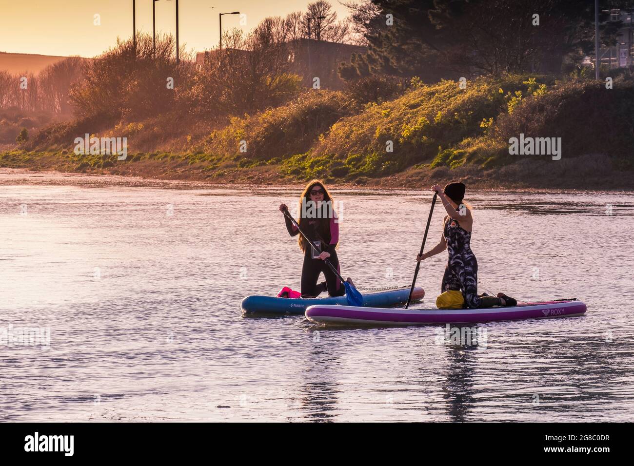 Golden evening light as two female paddle boarders on Stand Up ...