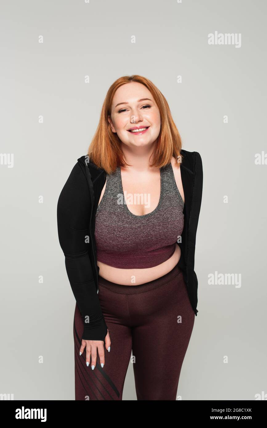 Happy body positive woman in sportswear looking at camera isolated on ...