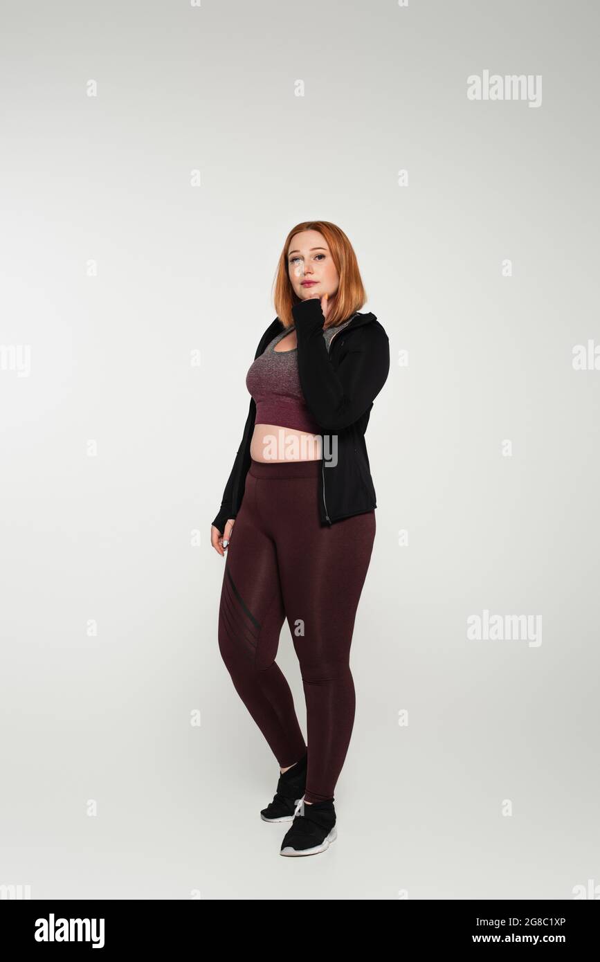Red haired plus size woman in sportswear standing on grey background ...