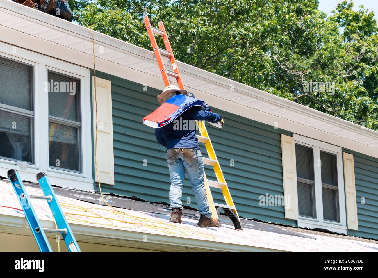 Man walking on a residential roof carrying a package of shingles ...