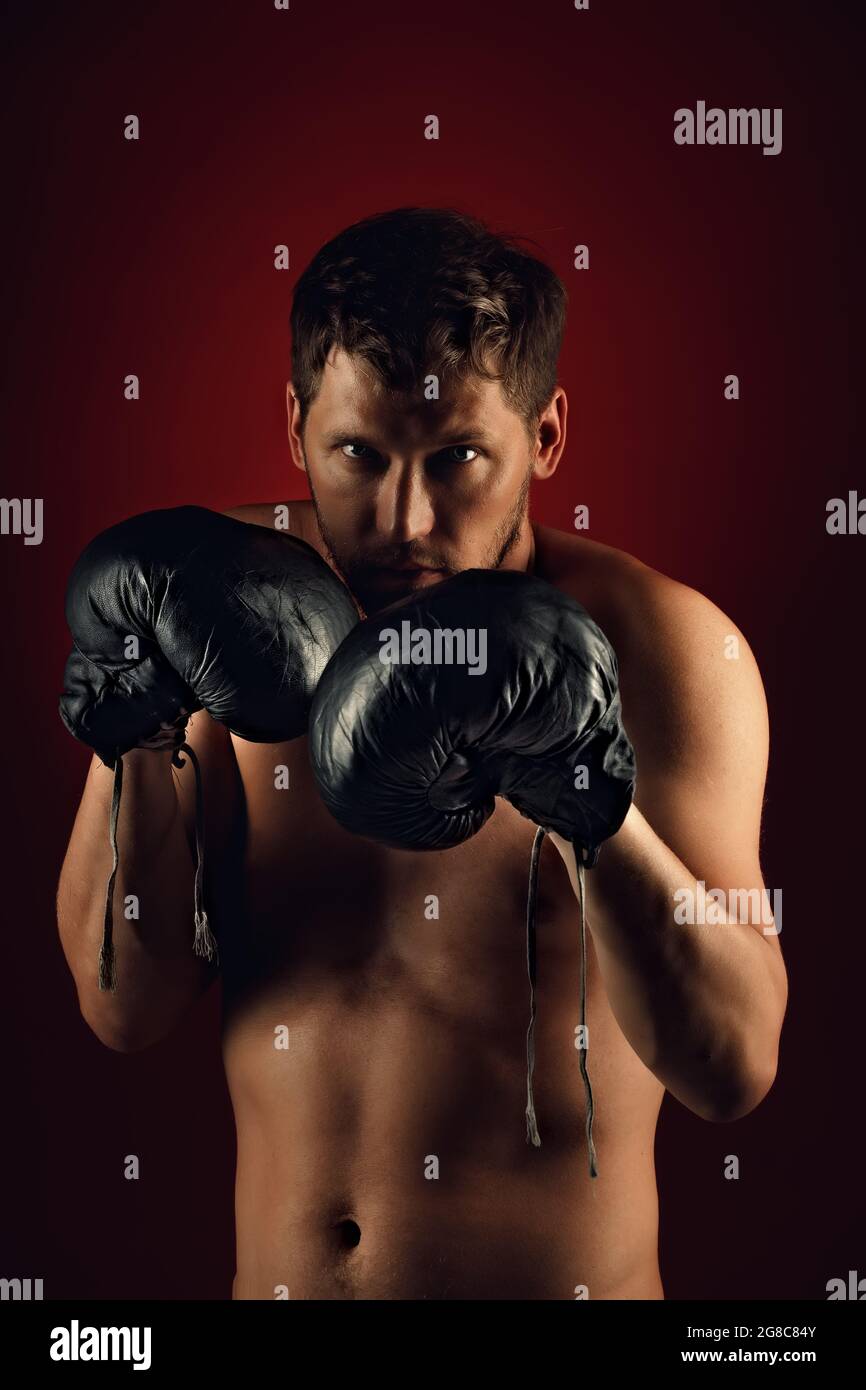 This is a dramatic portrait of a boxer in old boxing gloves on a dark ...