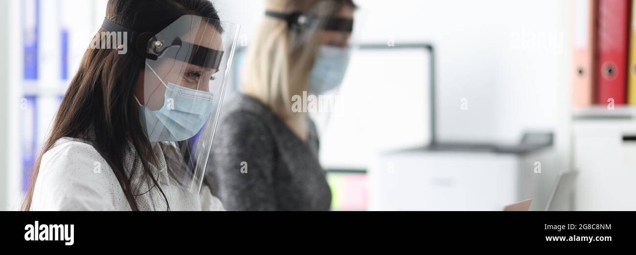 Women wearing protective masks and shields working at computers in ...