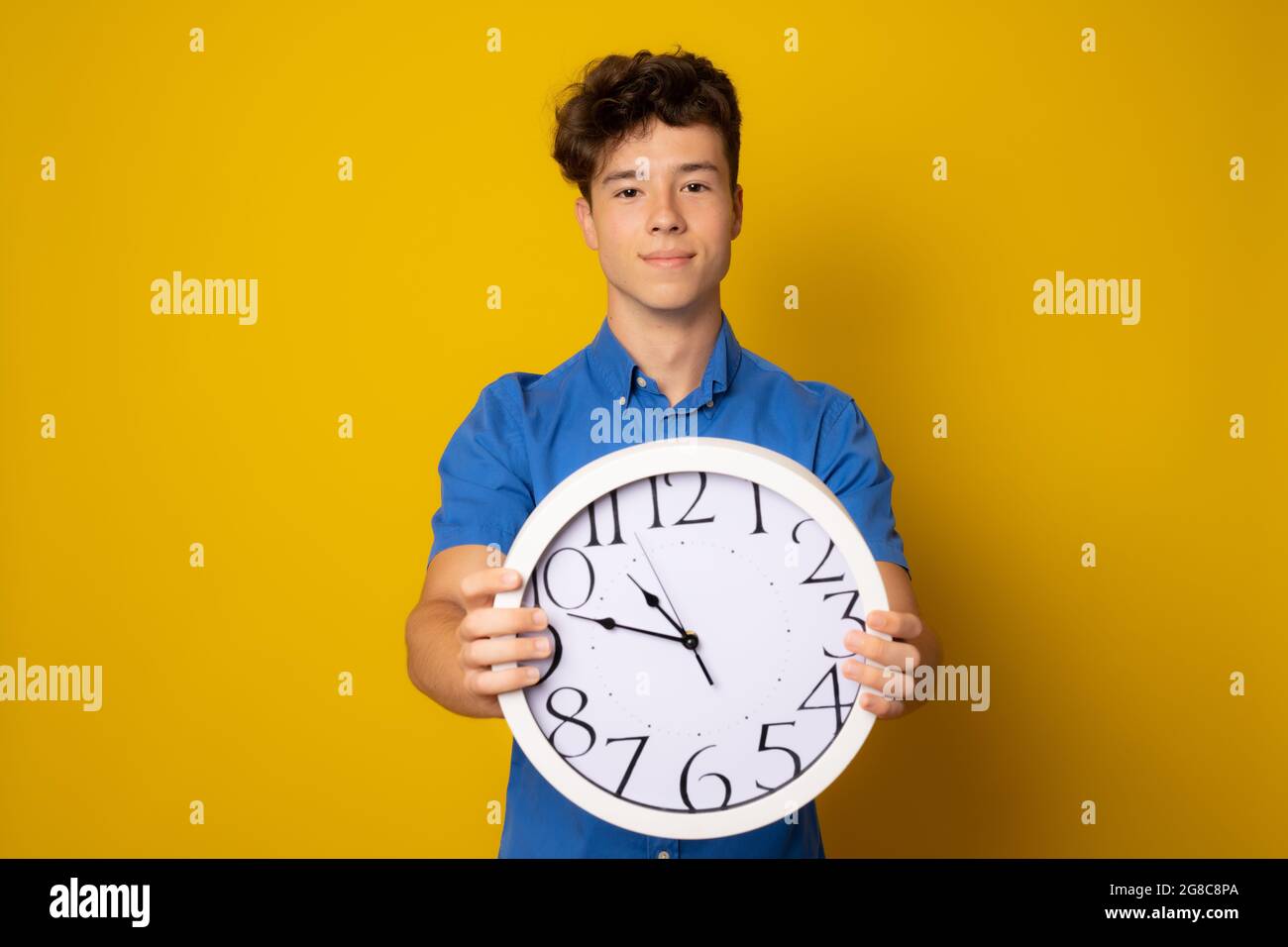 Portrait of caucasian teen boy with clock. Funny teenager showing clock ...