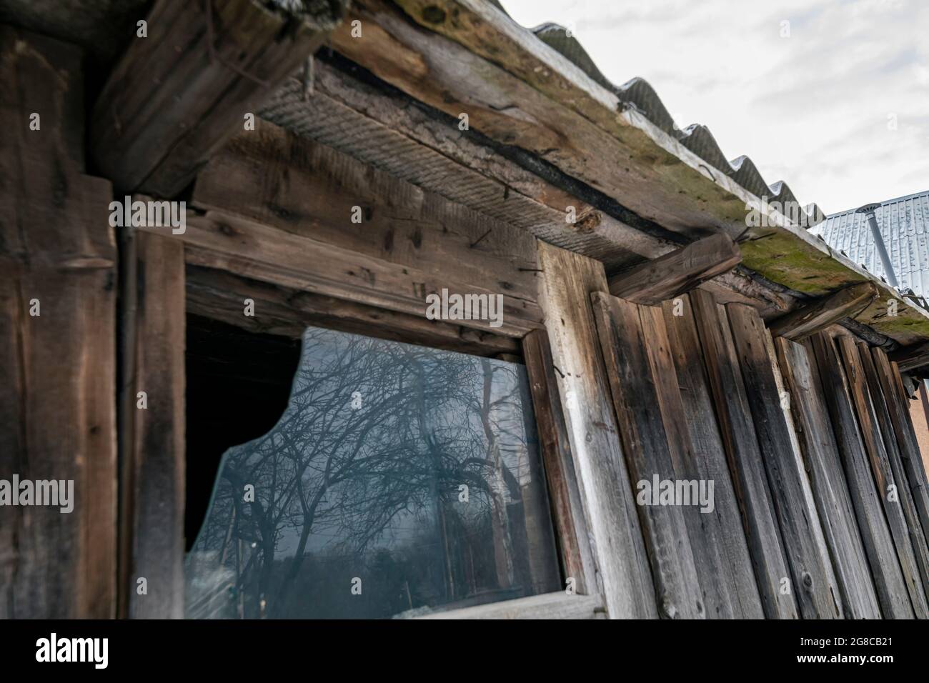 Broken window by an old wooden utility shed. Reflection of trees in the ...