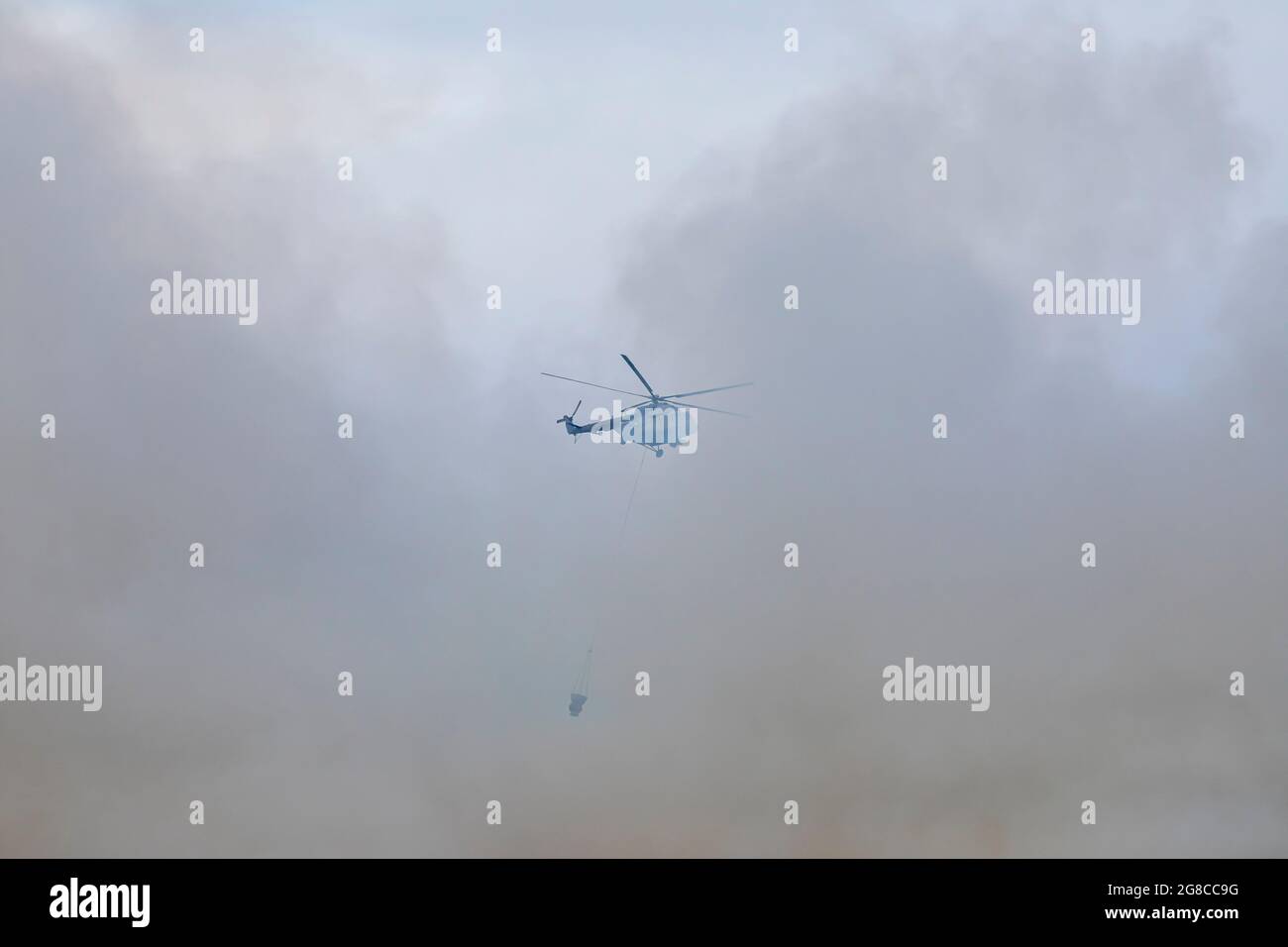 Firefighter helicopter with a water tank in smoke from a fire. Swirling ...