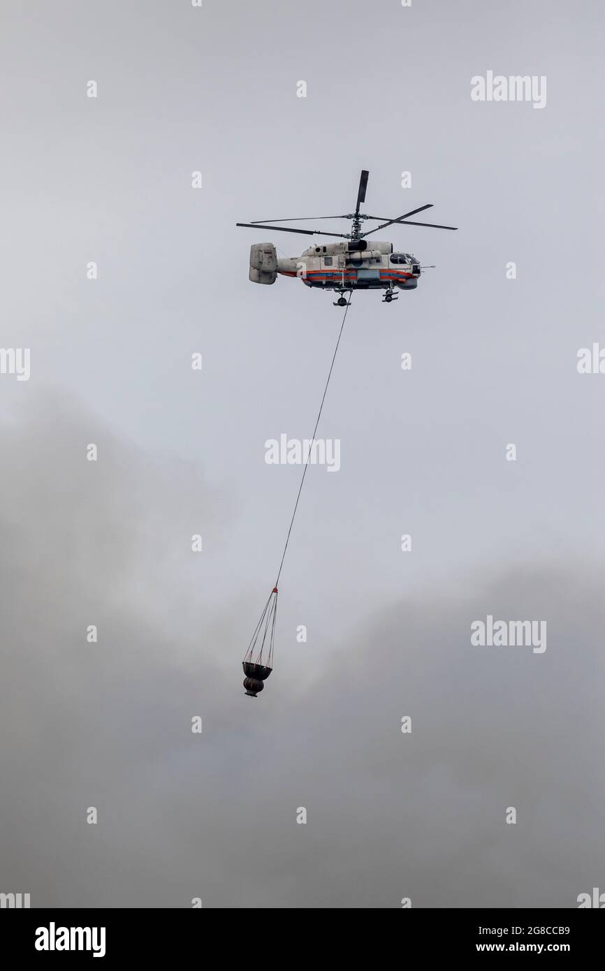 Firefighter helicopter with a water tank in smoke from a fire. Swirling ...