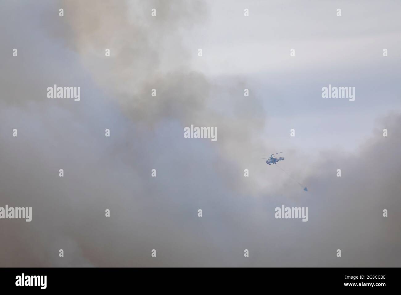 Firefighter helicopter with a water tank in smoke from a fire. Swirling ...