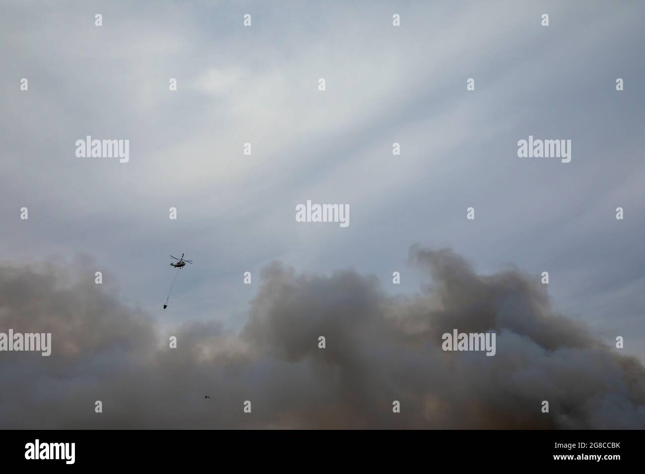 Firefighter helicopter with a water tank in smoke from a fire. Swirling ...