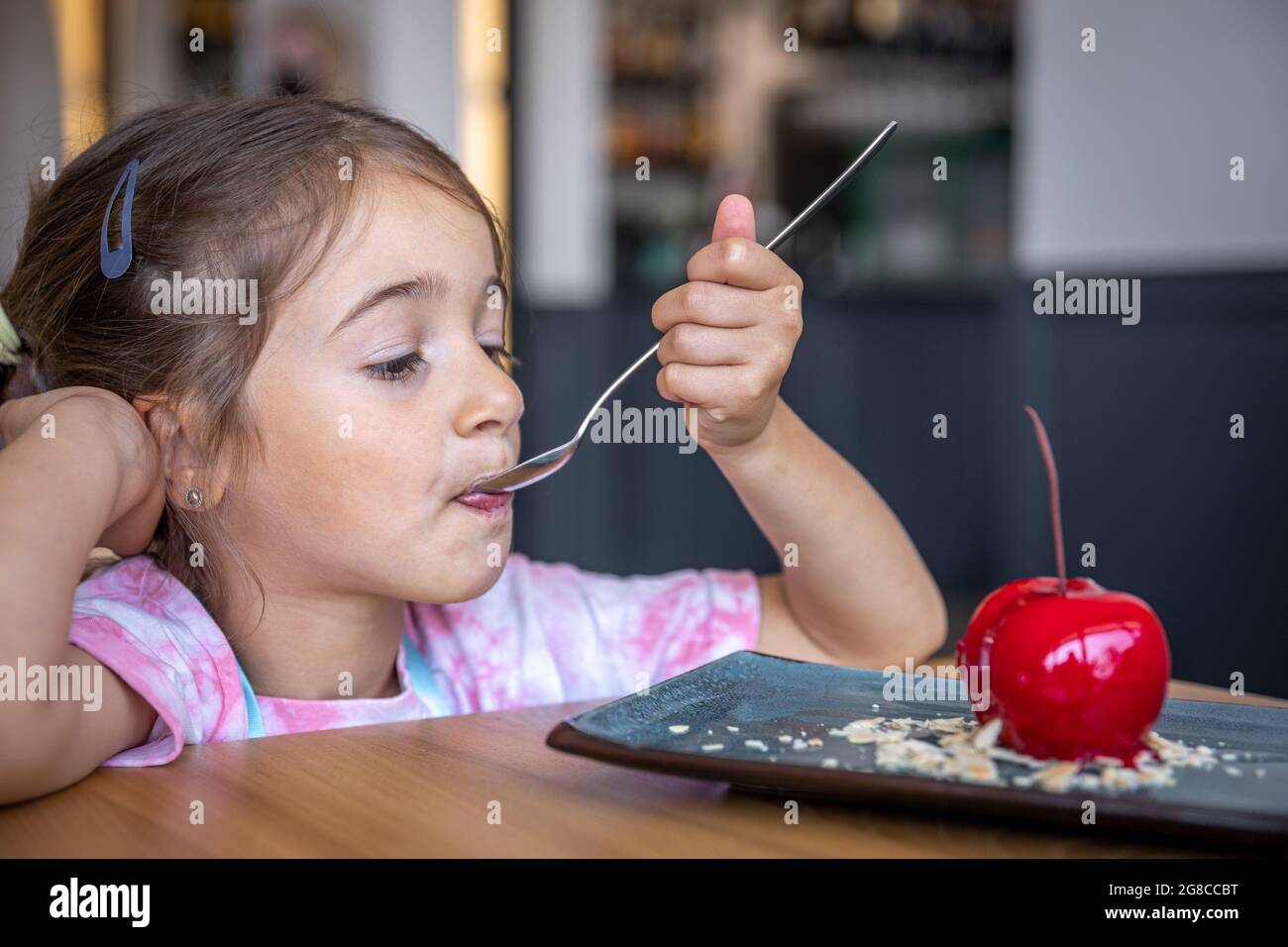 Cute little girl eating cherry-shaped chocolate mousse, french dessert ...
