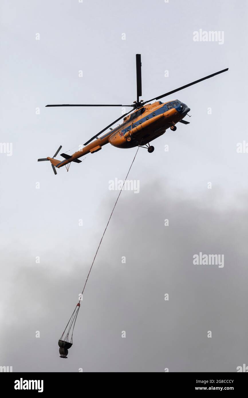 Firefighter helicopter with a water tank in smoke from a fire. Swirling ...