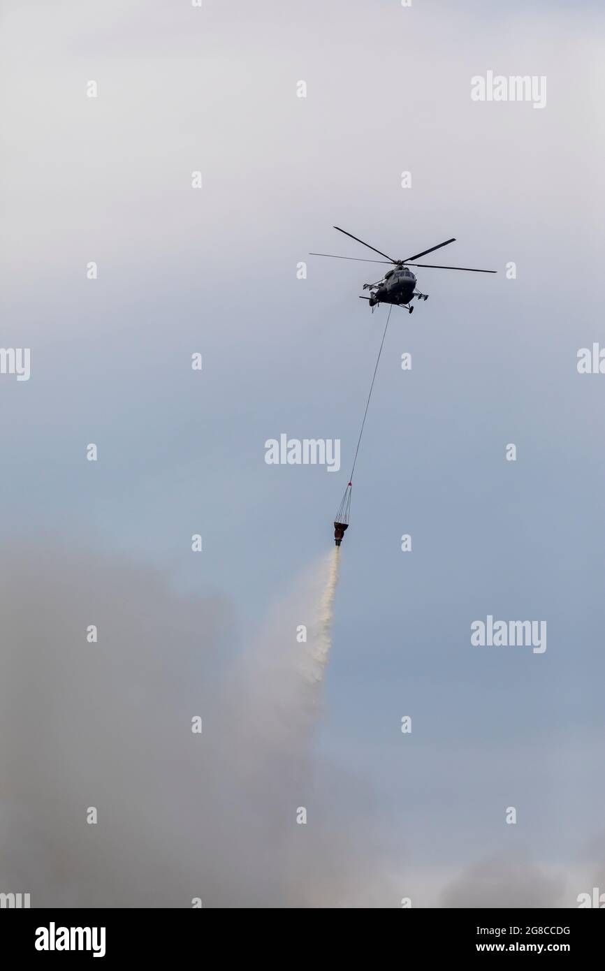 Firefighter helicopter with a water tank in smoke from a fire. Swirling ...