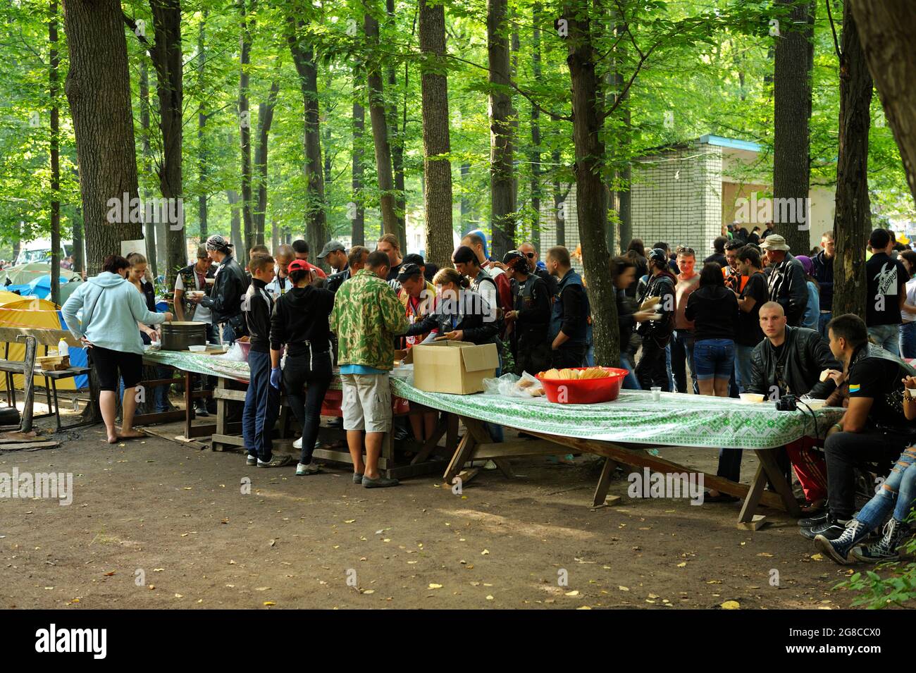 Crowd of people standing in a line for free food prepared on the field ...