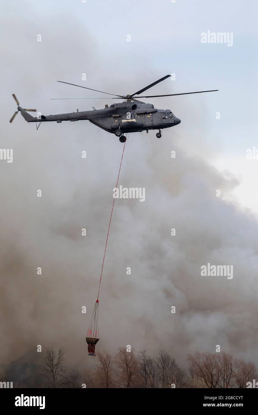 Firefighter helicopter with a water tank in smoke from a fire. Trees in ...