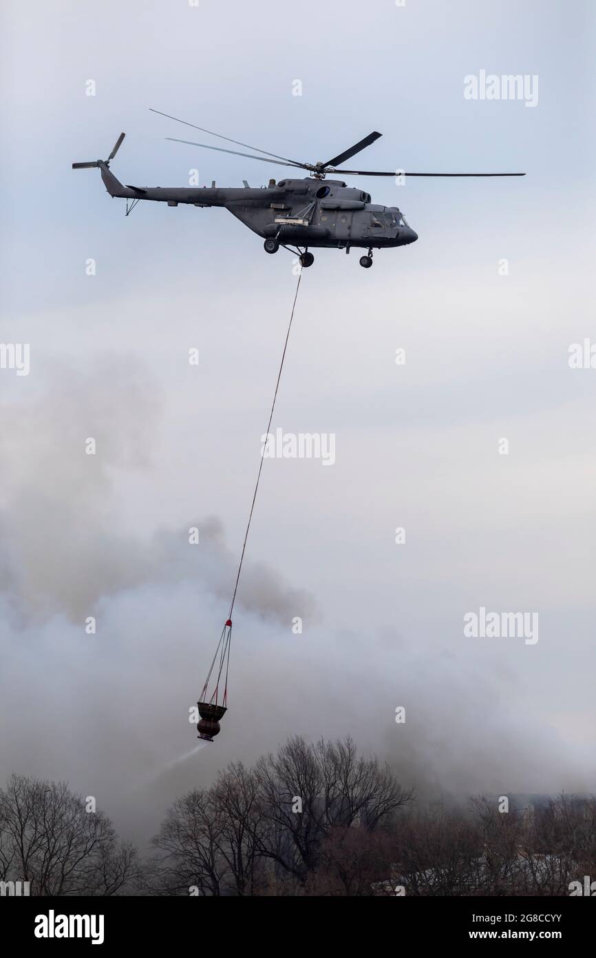 Firefighter helicopter with a water tank in smoke from a fire. Trees in ...