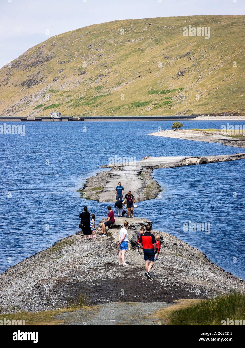 People walk along a pathway exposed by the falling water level at ...
