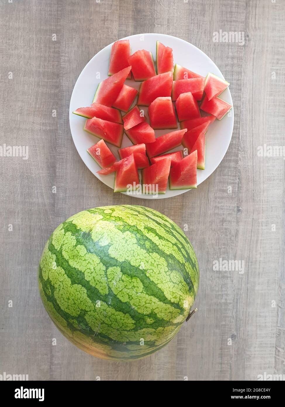 A portrait of an uncut big green and round watermelon next to a white ...