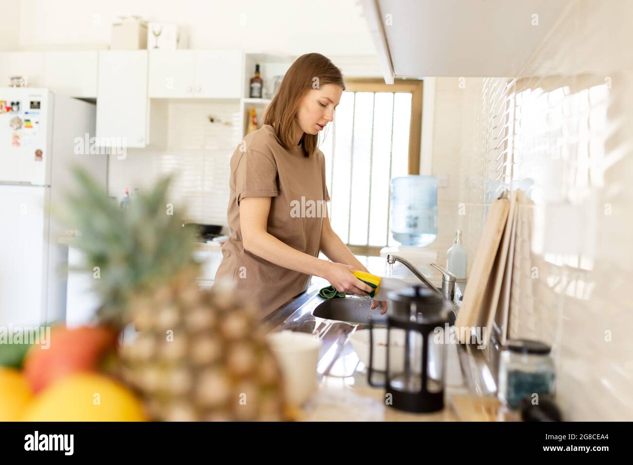 woman in home t shirt washing plates with sponge in domestic kitchen ...
