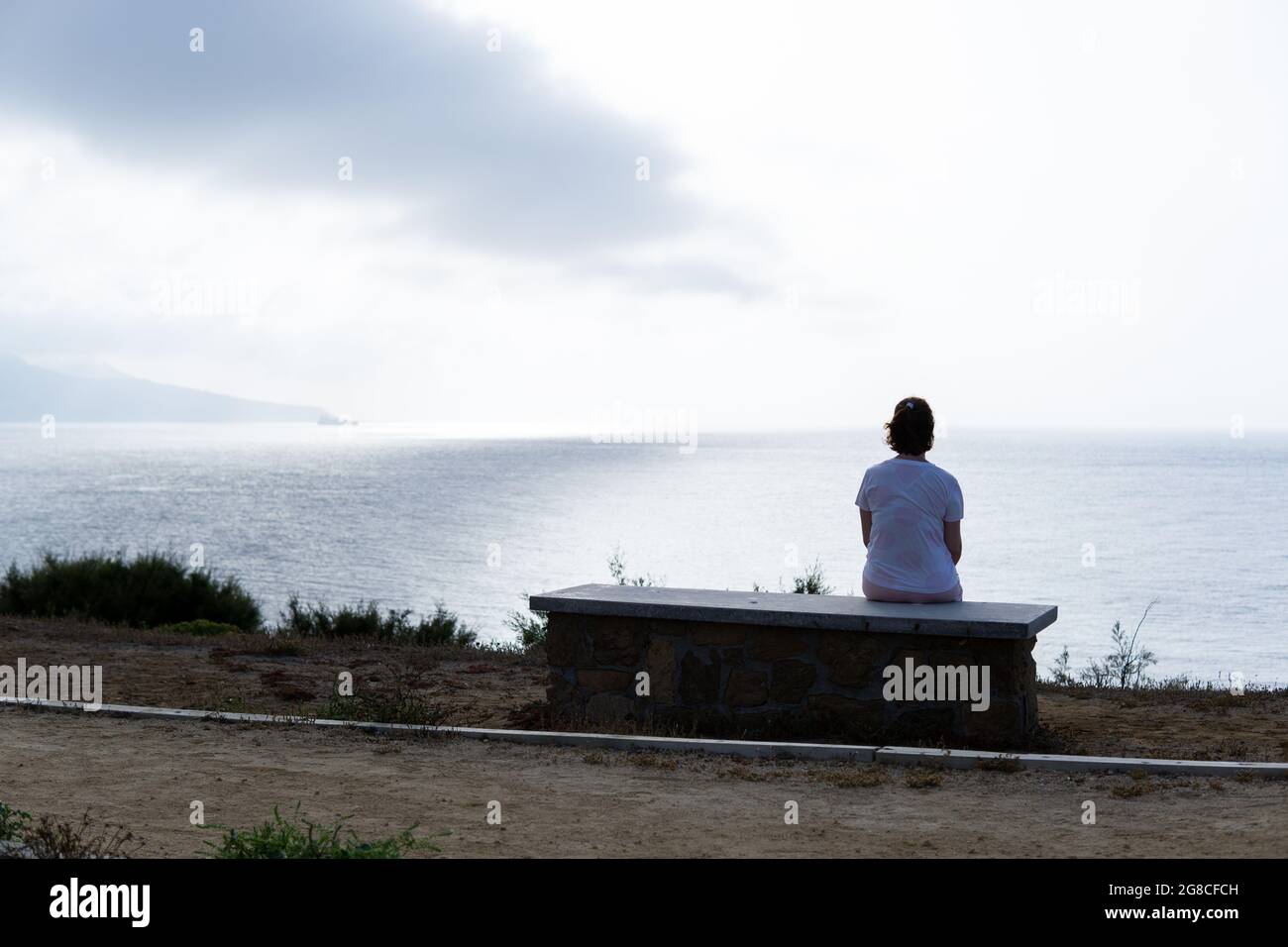 Woman sitting on a stone bench looking at the horizon on a sad a Stock ...