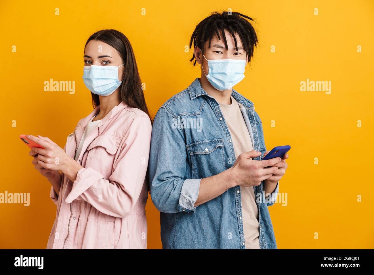 Young multiracial couple in face masks using mobile phones isolated ...