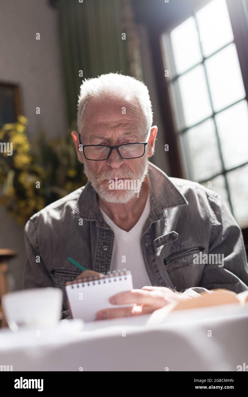 Senior man taking notes at home, hard light effect Stock Photo - Alamy