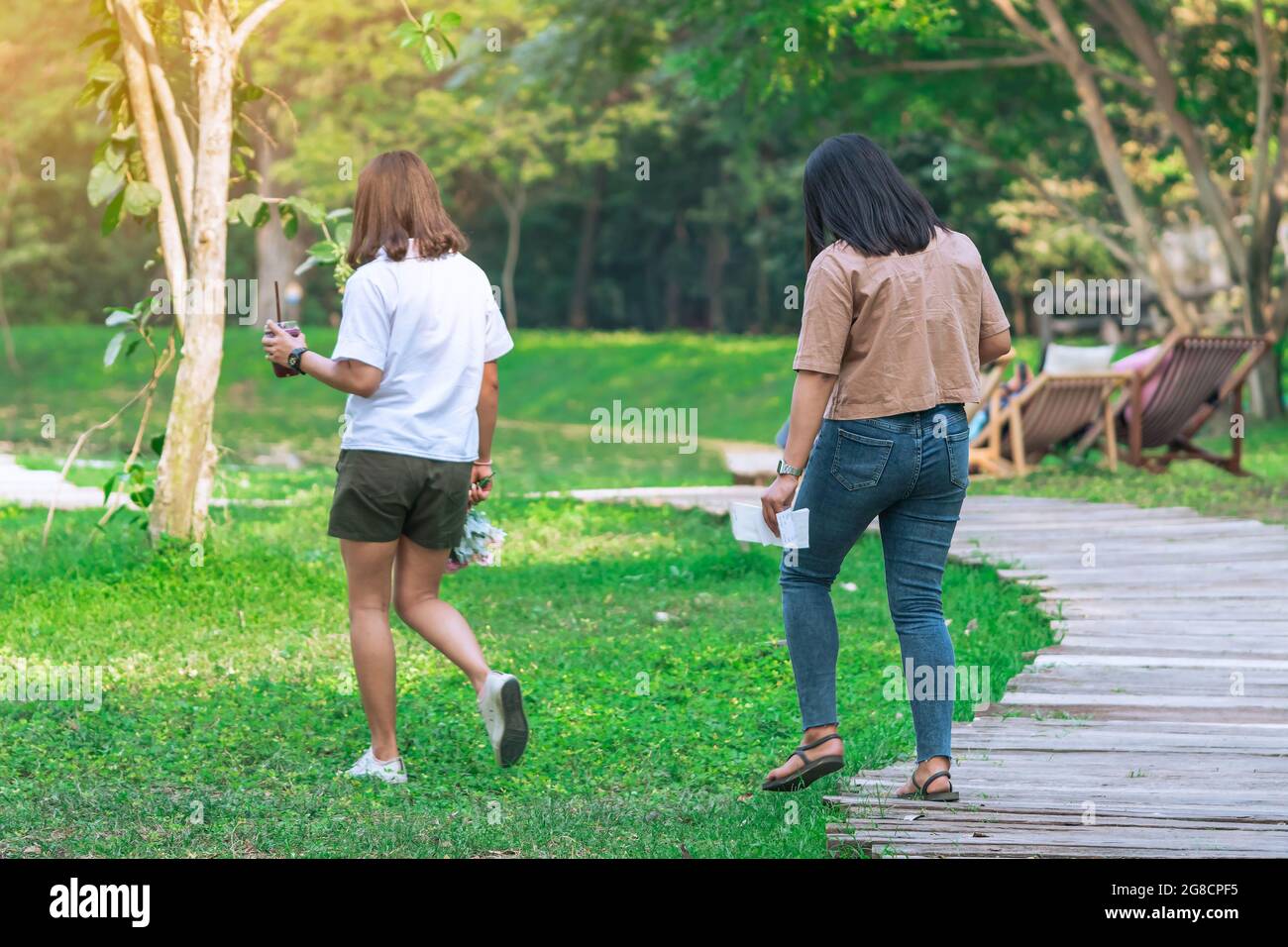 Back view of Asian women walking on pathway through green garden. Two ...