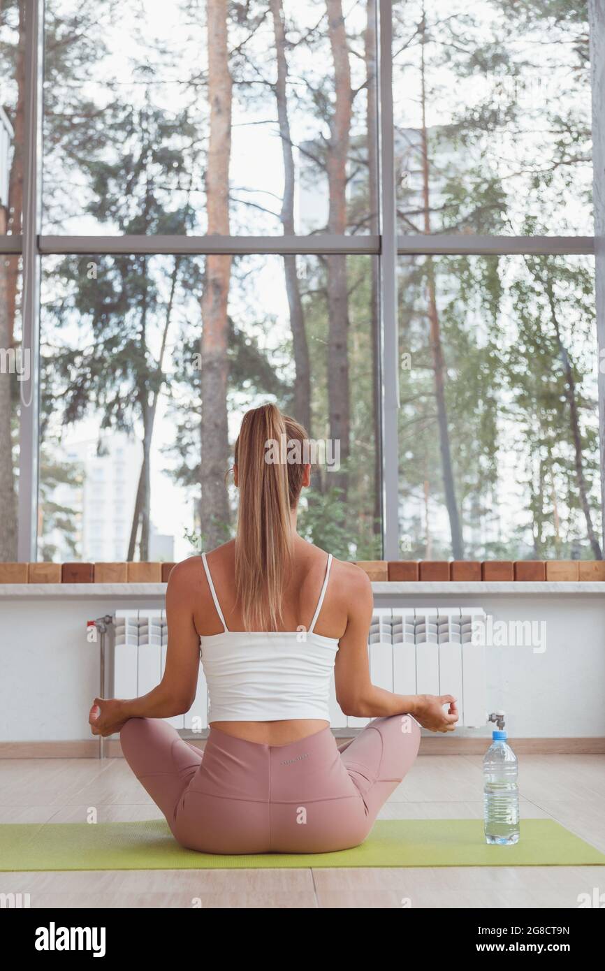 Yoga woman back view meditate sitting in lotus pose over big windows ...