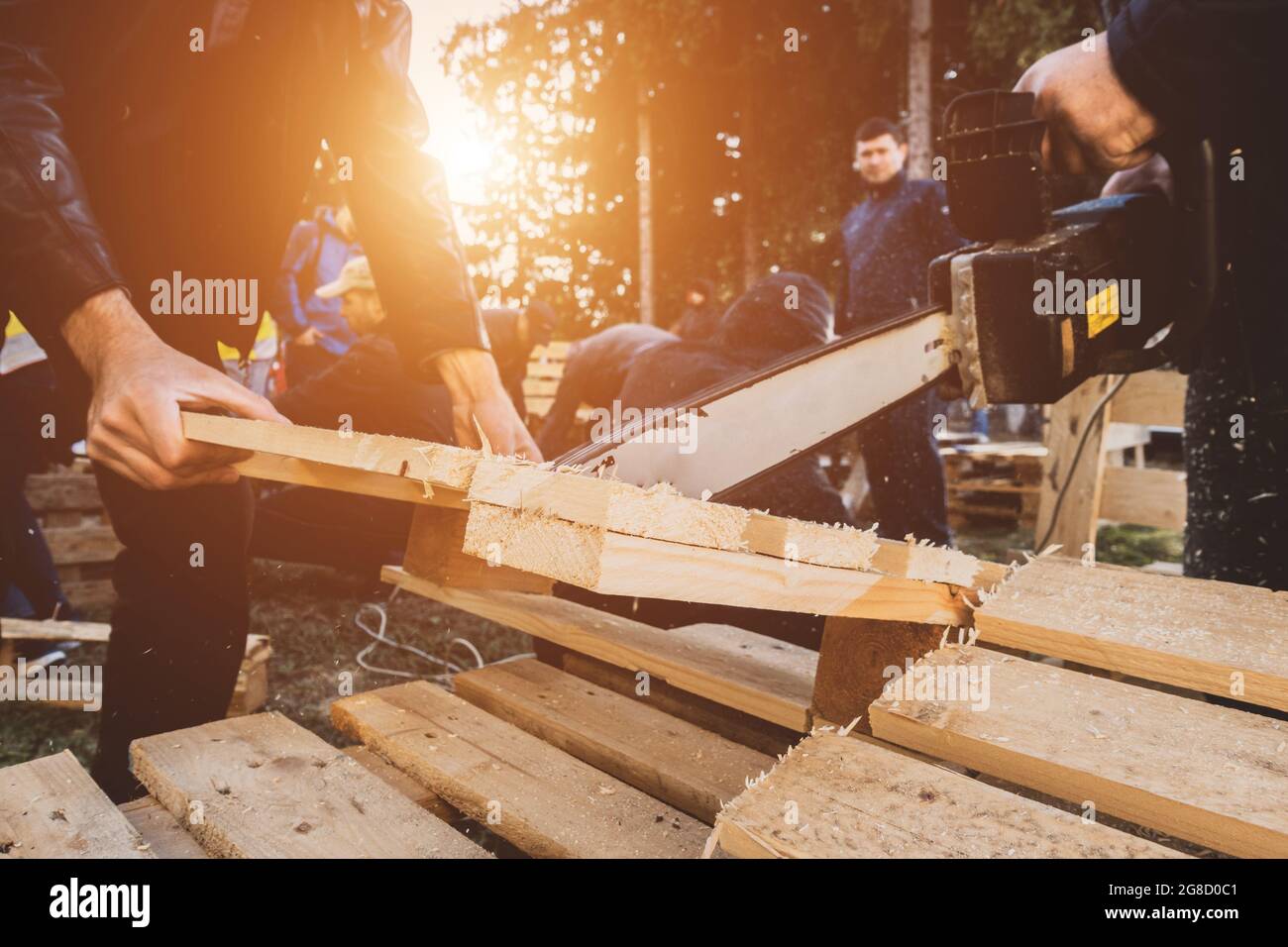 A man sawing a wooden pallet with a chainsaw. Making outdoor furniture ...
