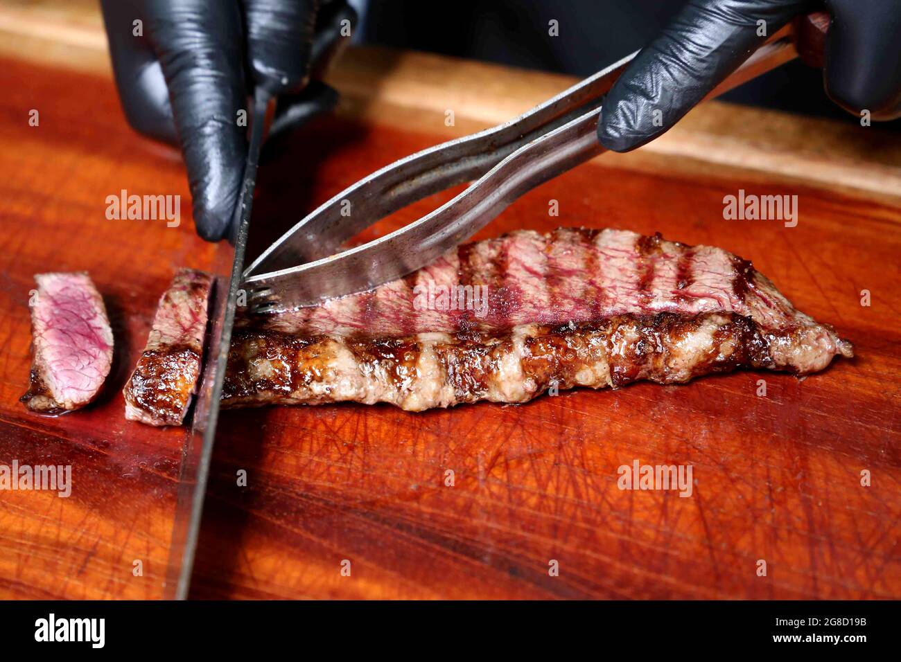 Picanha or Rump Steak. Hand with black gloves cutting a juicy steak on ...