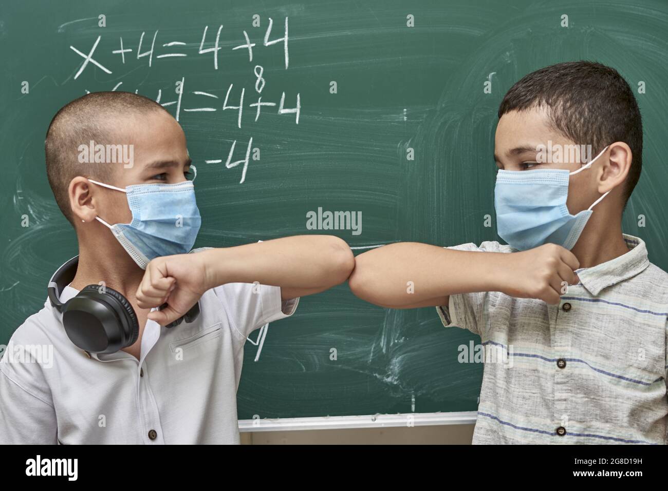 Young male classmates wearing facemasks and elbow bumping in the ...