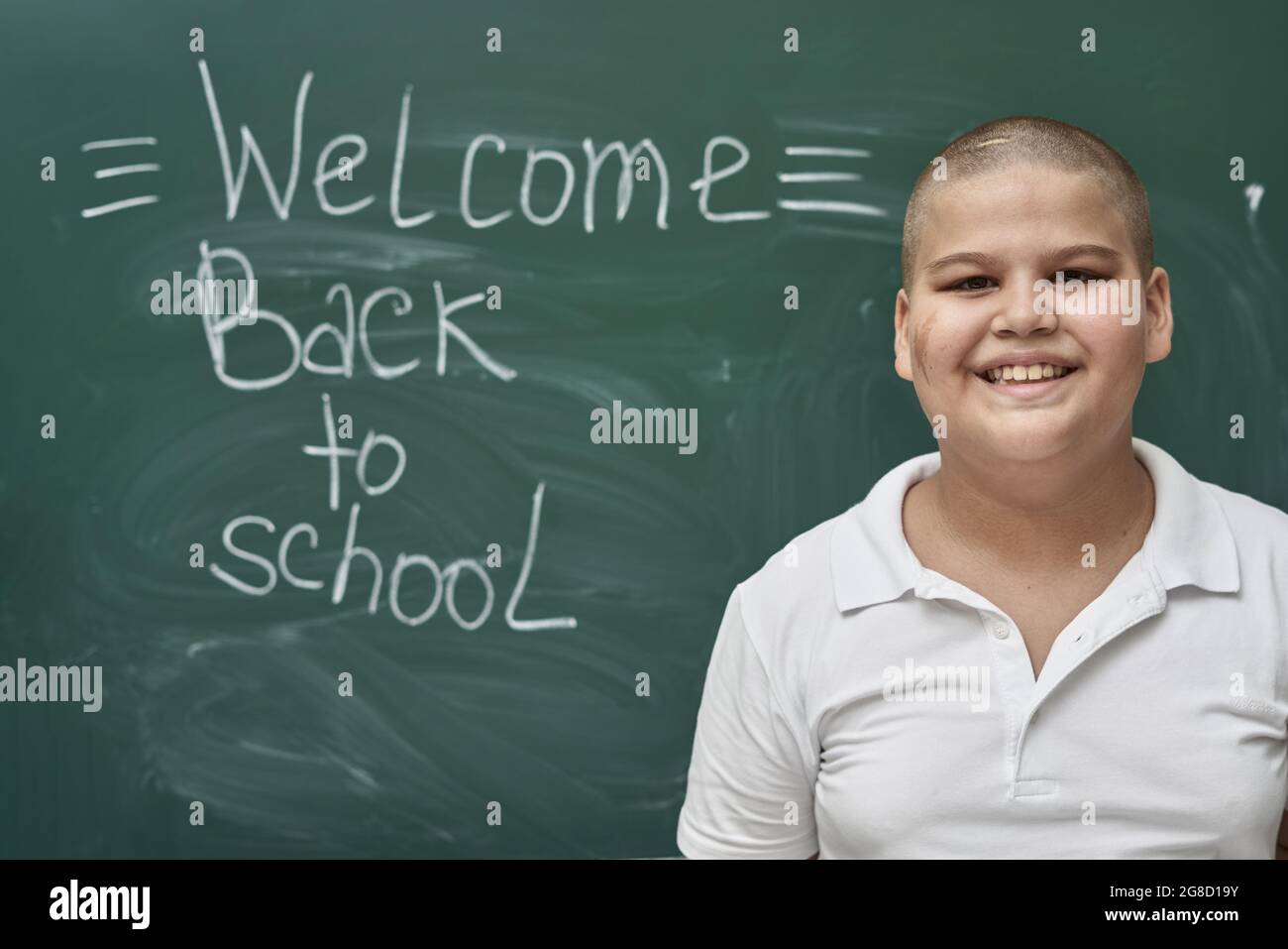 Young male pupil standing near the blackboard with "Welcome back to ...