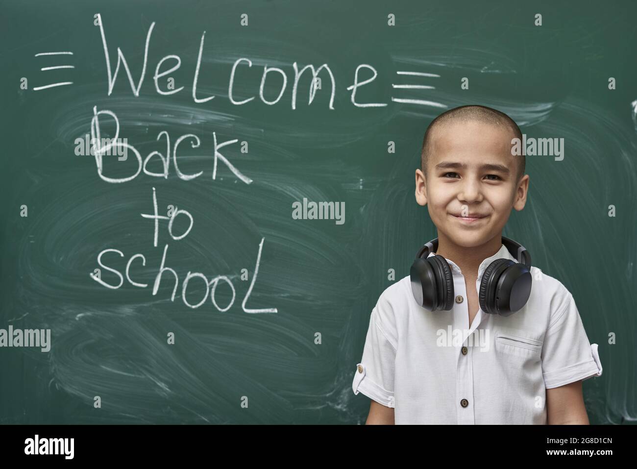 Young male pupil standing near the blackboard with "Welcome back to ...