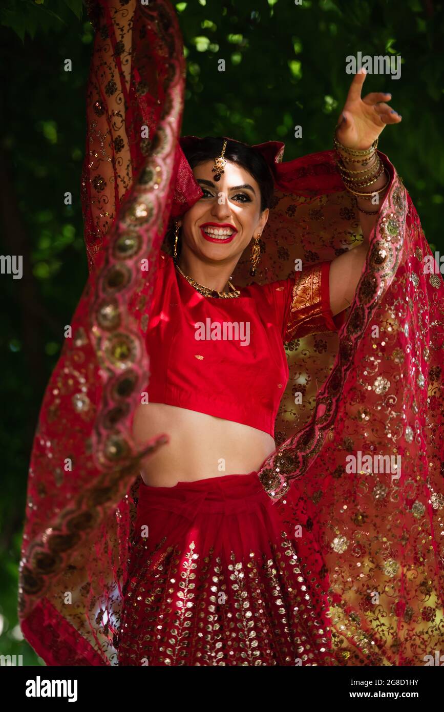 happy indian bride in red sari and traditional headscarf with ornament ...