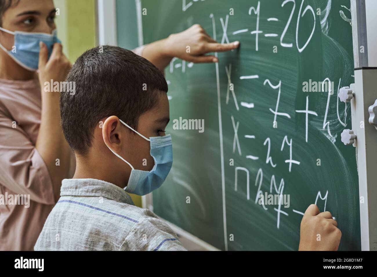 Multi-racial teacher wearing a facemask and explaining a math formula ...