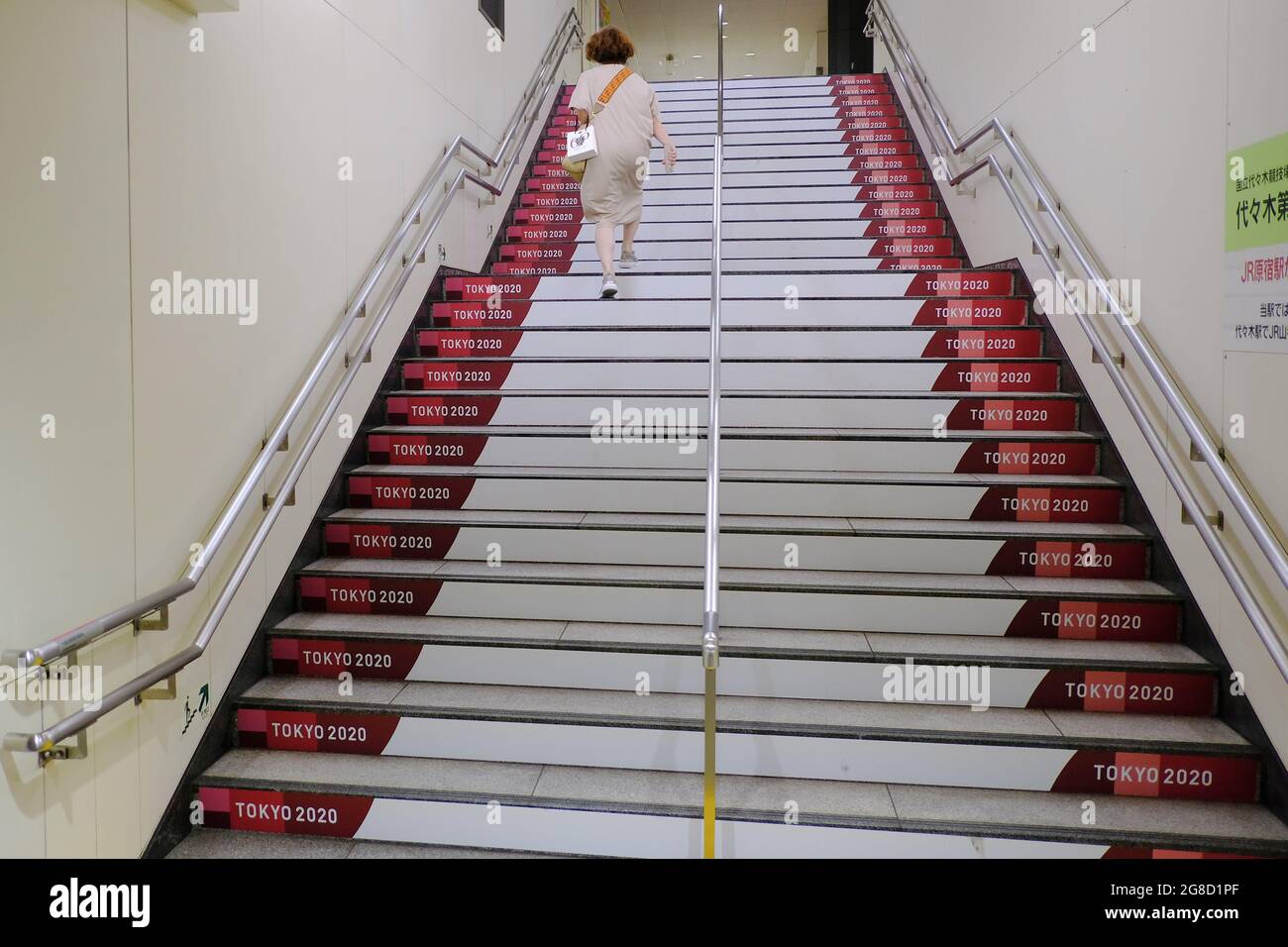 A woman climbs the stairs with an Olympic banner affixed at a subway ...