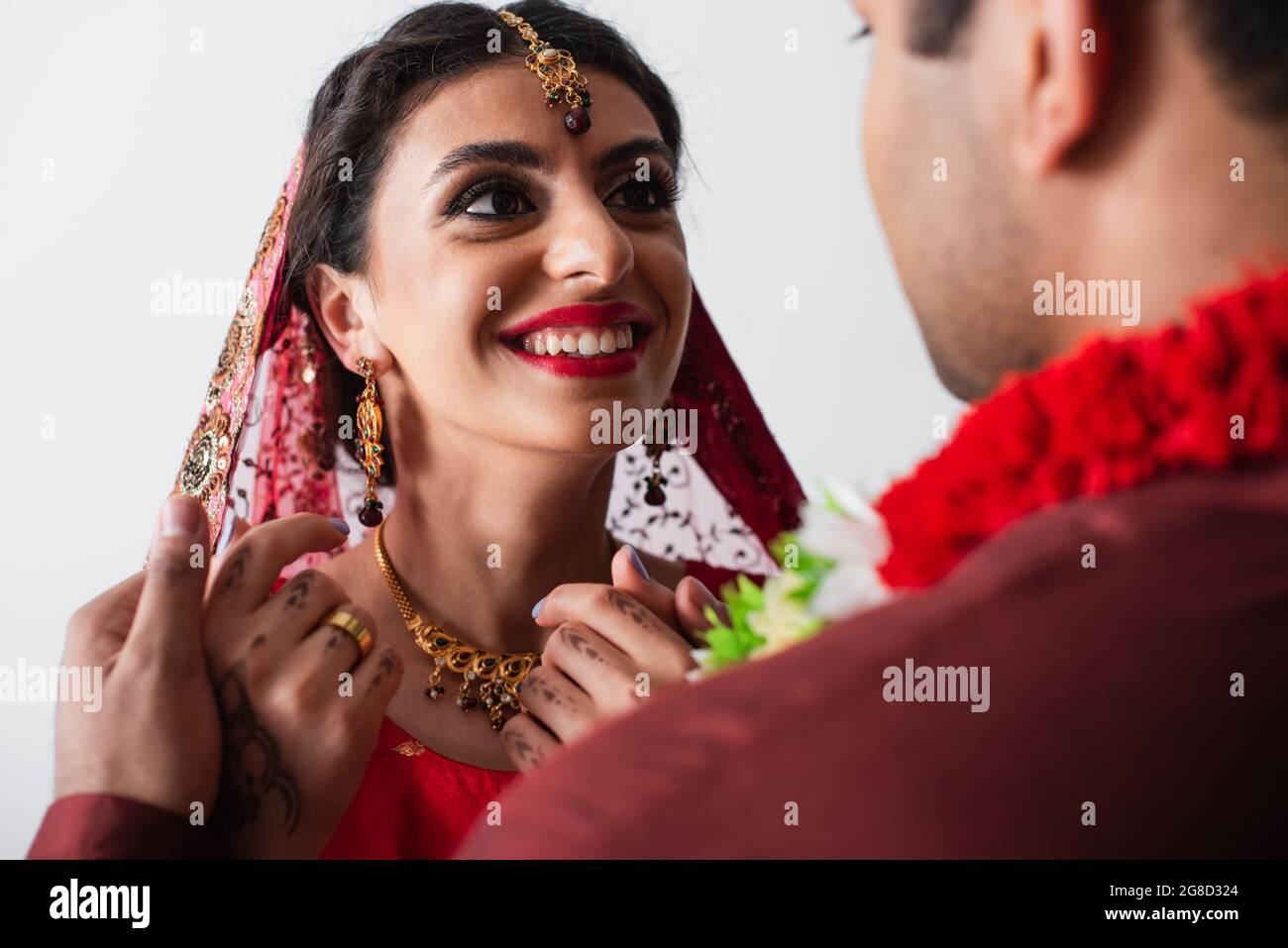 happy indian bride in headscarf looking at blurred bridegroom isolated ...