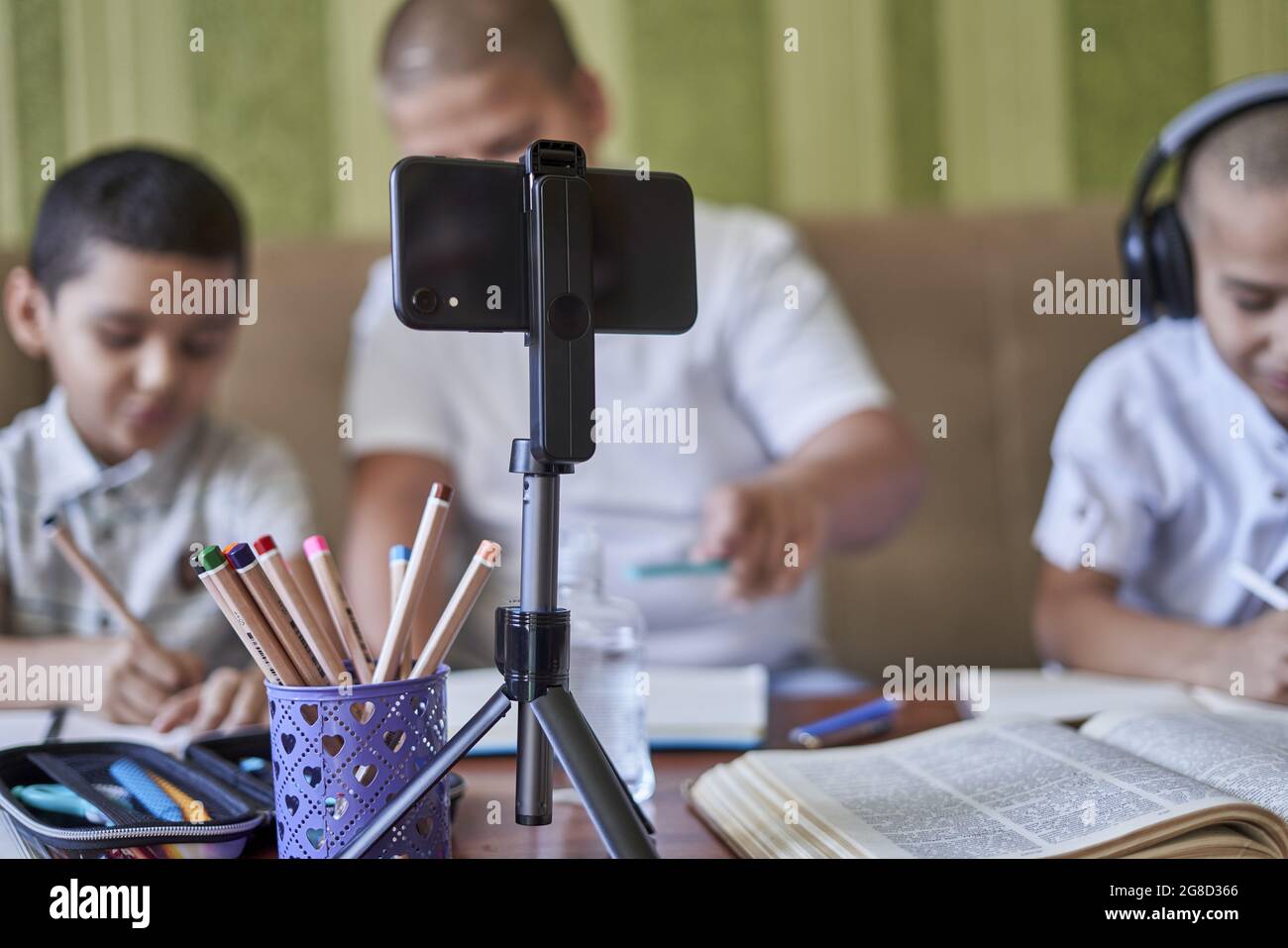 Phone on a stand on the table with pupils listening to an online class ...