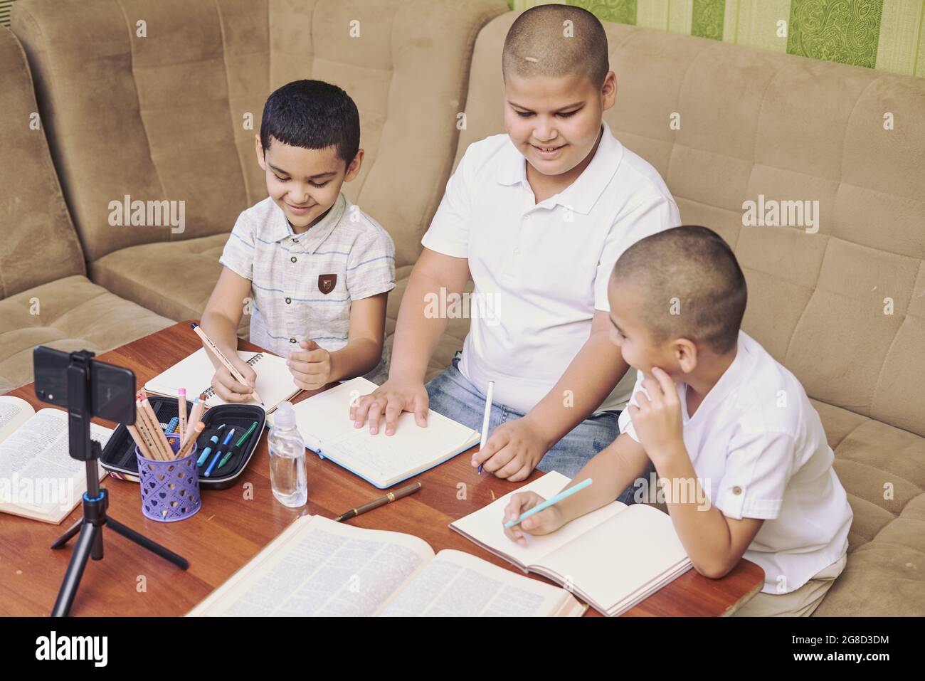 Male pupils writing in their textbooks during an online class at home ...