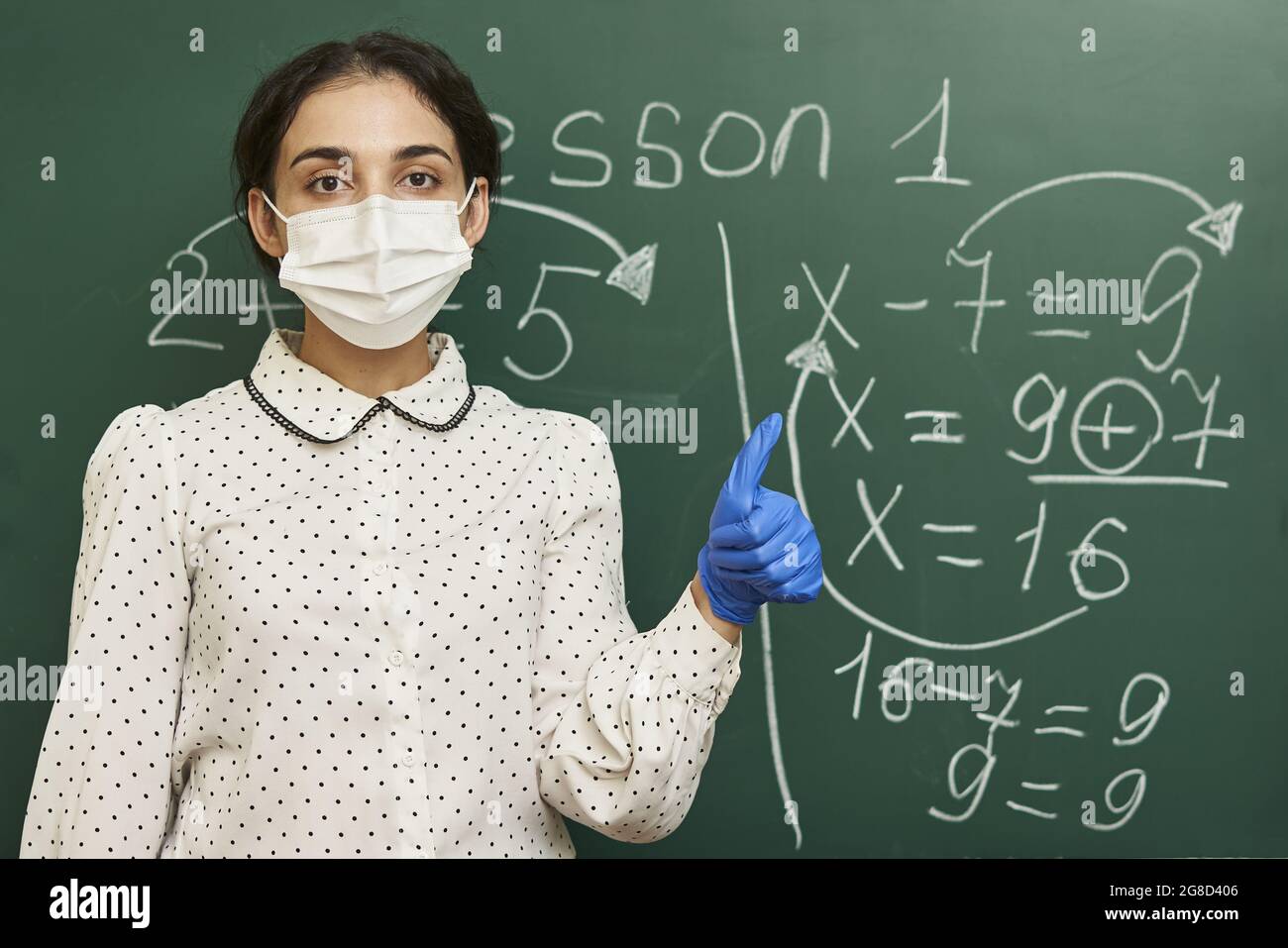 Female teacher wearing a facemask with latex gloves and explaining a ...